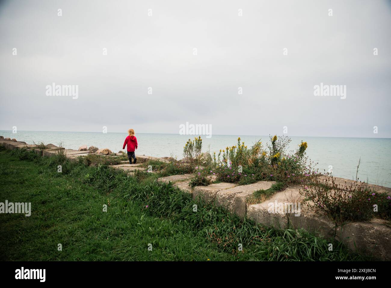 Child walking on a concrete path by Lake Huron, wearing a red jacket ...