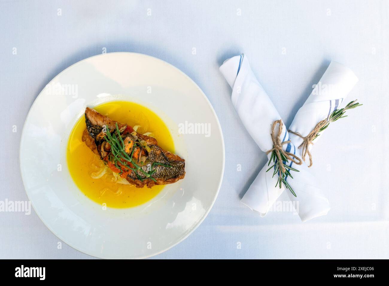 Overhead view of fish entree on white table linen with flatware rolls ...
