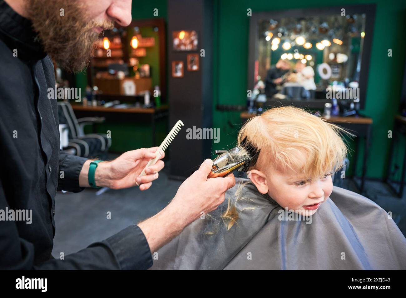 Professional hairdresser shaving boy's head, using shaver and comb ...