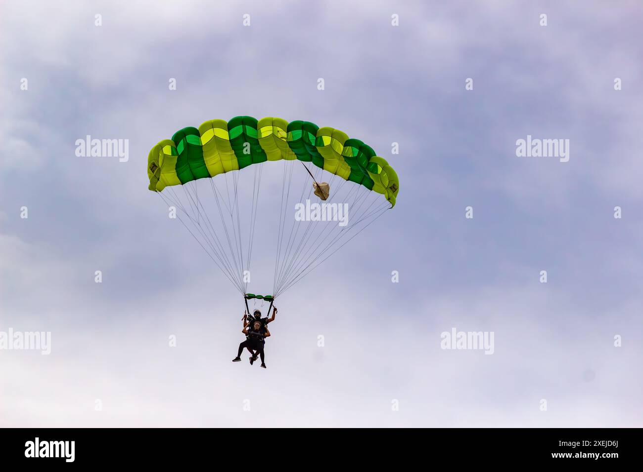 Tandem skydivers with a green parachute descending in a cloudy sky ...