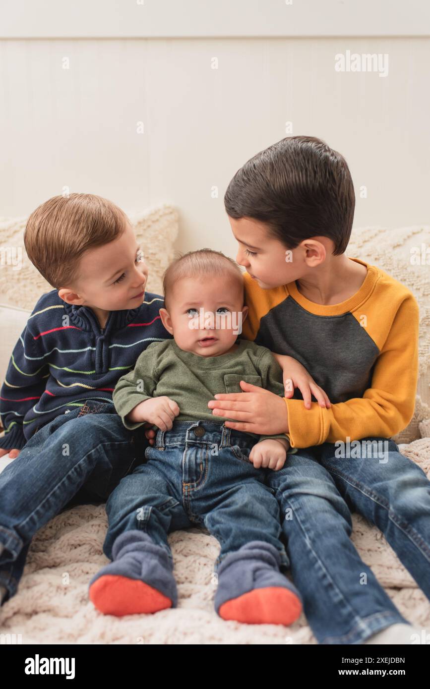 Toddler brothers comforting crying baby brother while sitting on bed ...