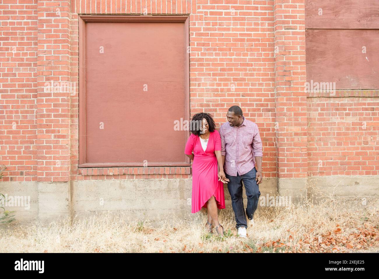 Couple leaning against red brick wall laughing Stock Photo - Alamy