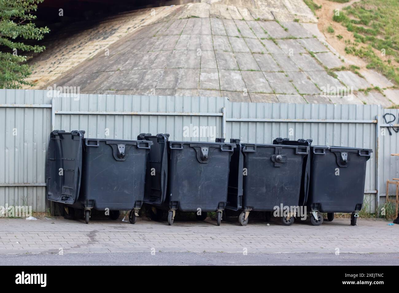 A row of black waste containers are placed in front of a wall, on ...