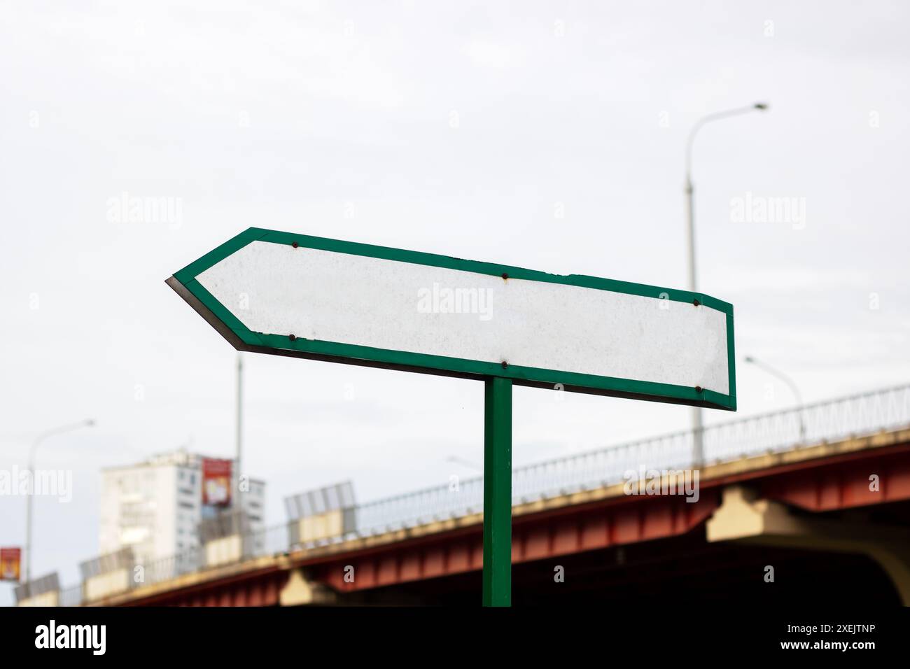 A green and white sign with an arrow, located in front of a bridge ...