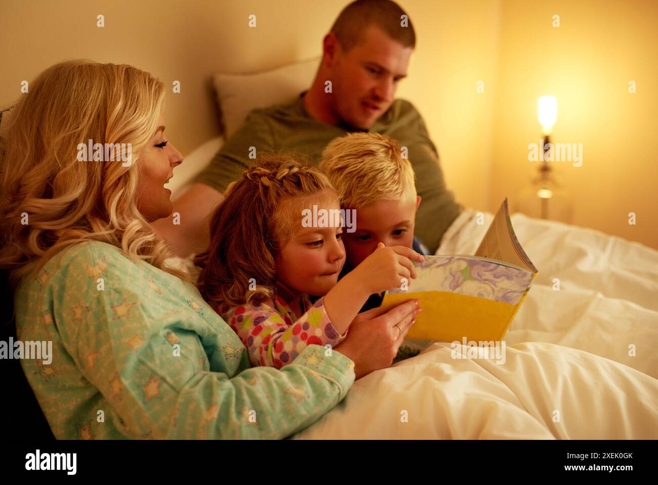Bed, parents and children with book for reading story, bonding together ...