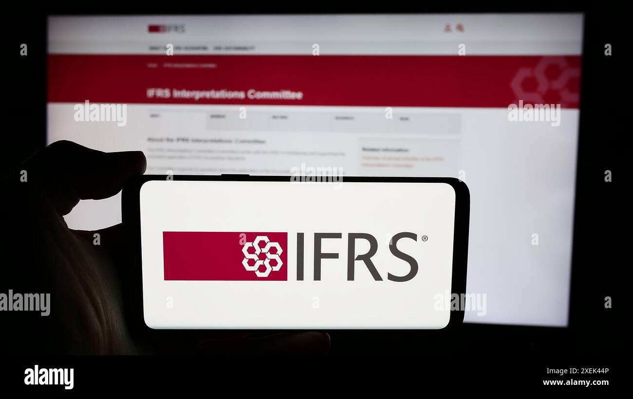 Person holding cellphone with logo of International Financial Reporting Standards Foundation ...