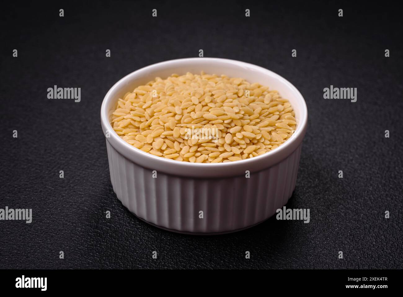 Raw risoni pasta made from durum wheat on a dark concrete background ...