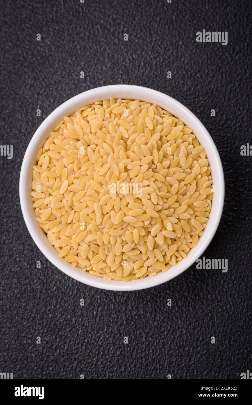 Raw risoni pasta made from durum wheat on a dark concrete background ...