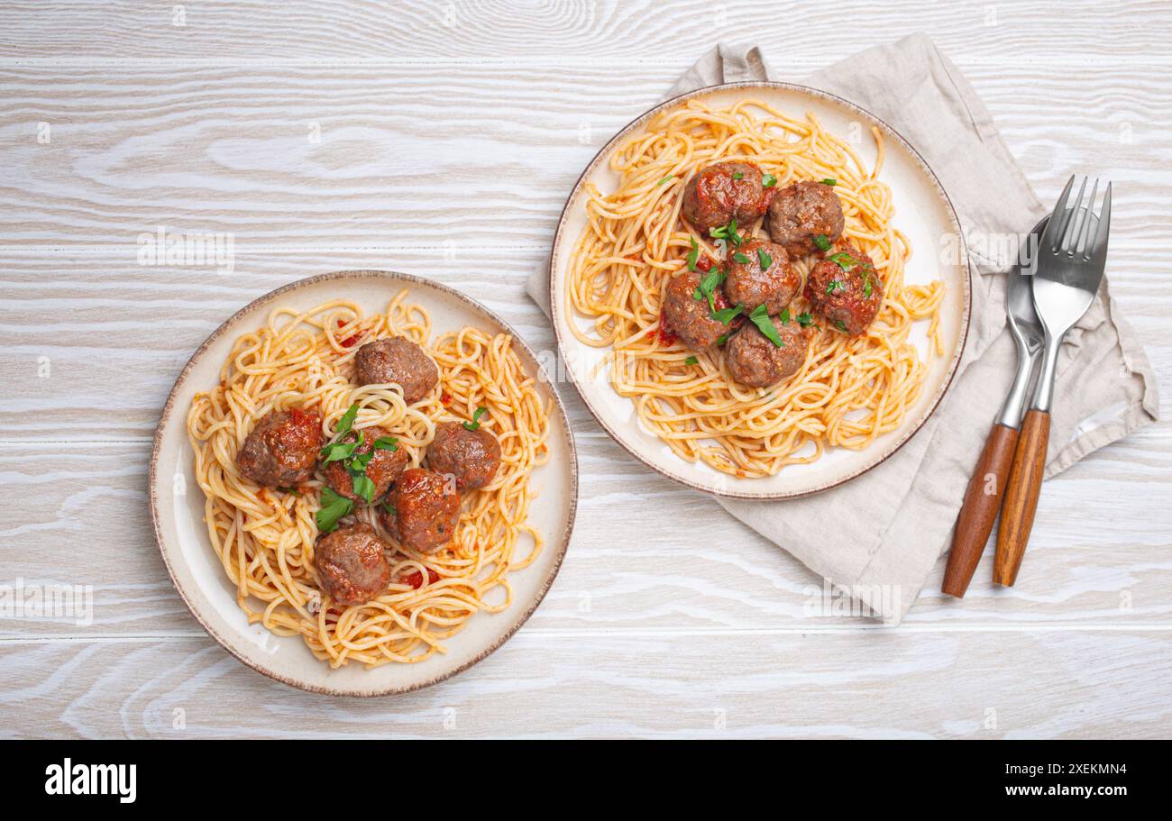 Two plates of delicious spaghetti with meatballs served on white wooden ...