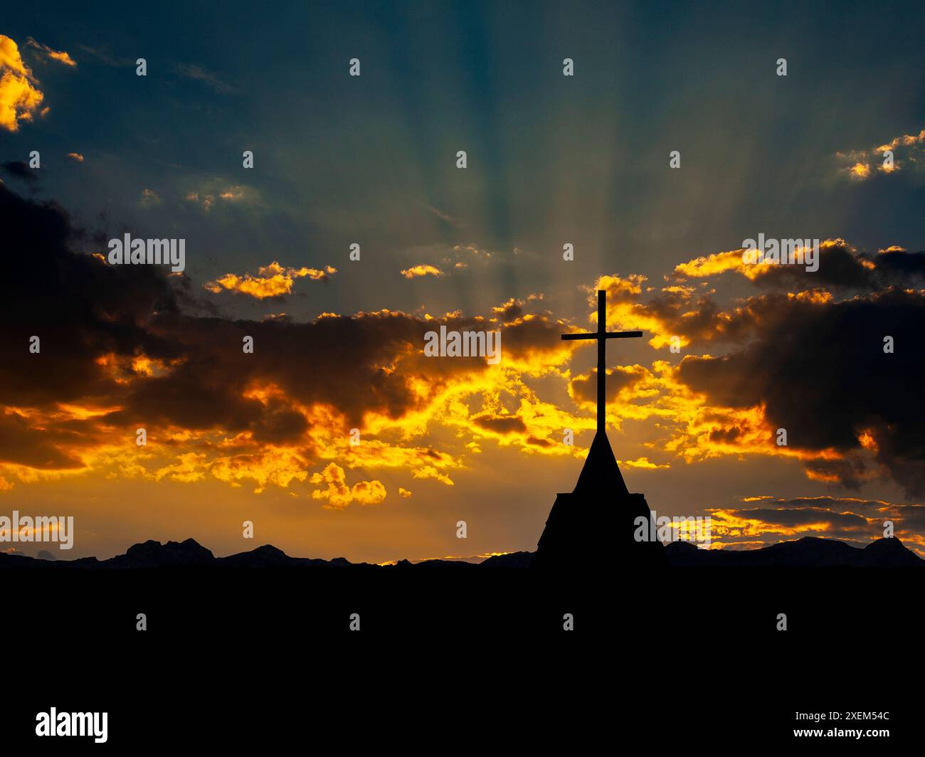Silhouette of a church steeple's cross against a dramatic colourful sky ...