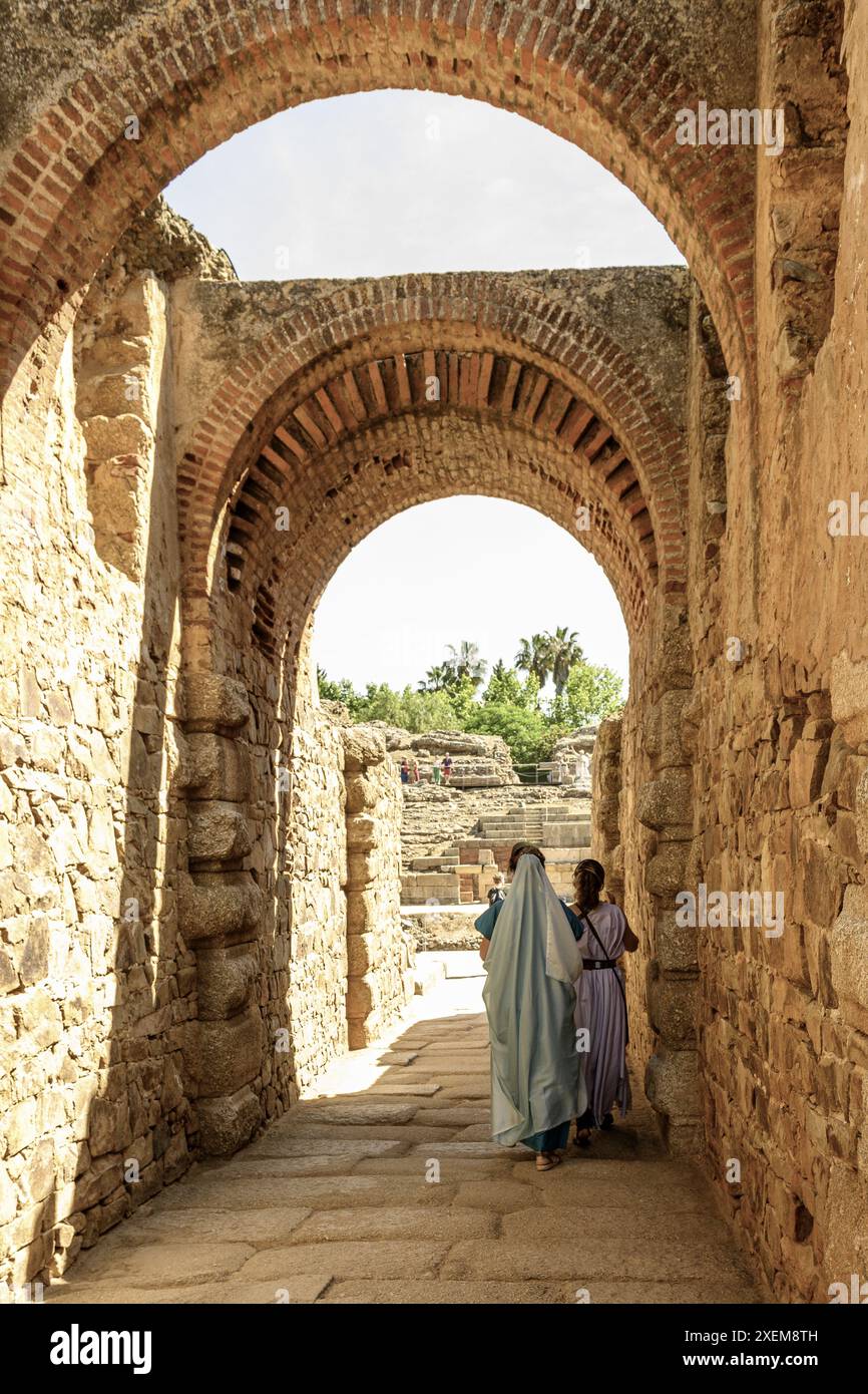 Two women dressed in Roman attire walk through a historic stone archway ...