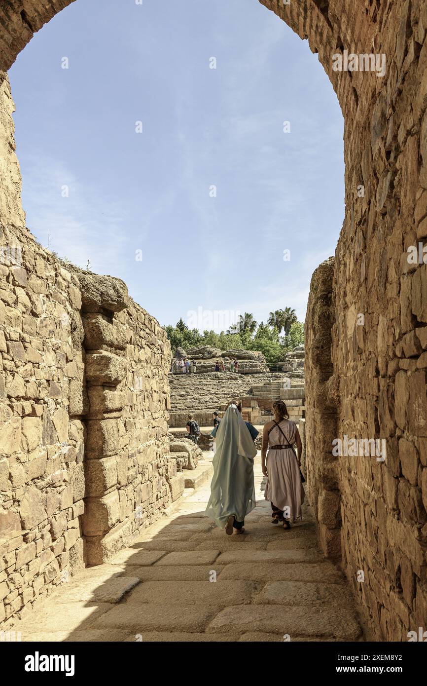 Two women dressed in Roman attire walk through a historic stone archway ...