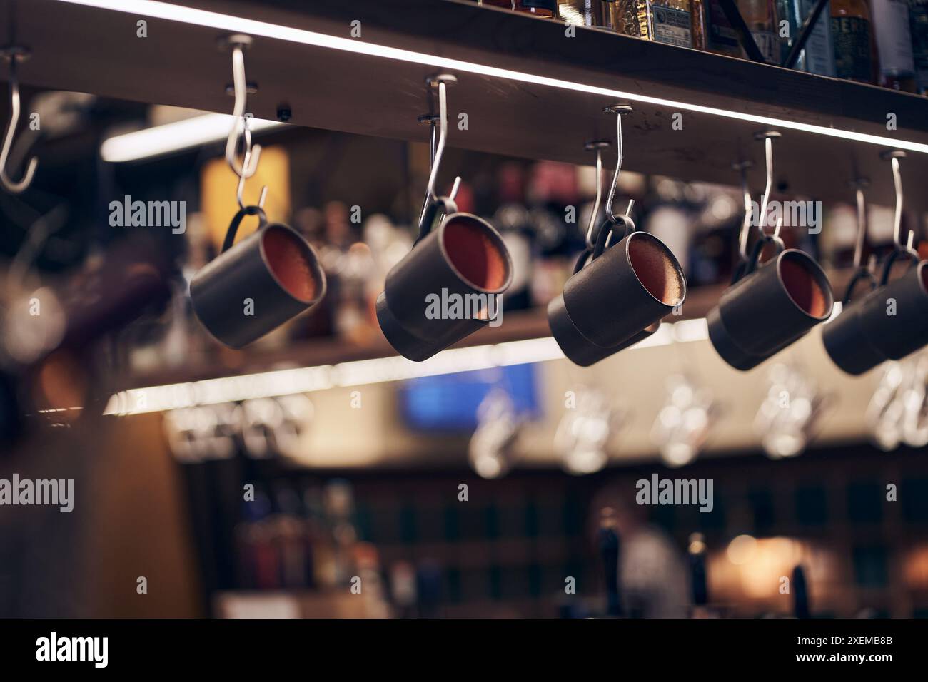 Ceramic mugs hanging on hooks under open shelves, on a defocused ...