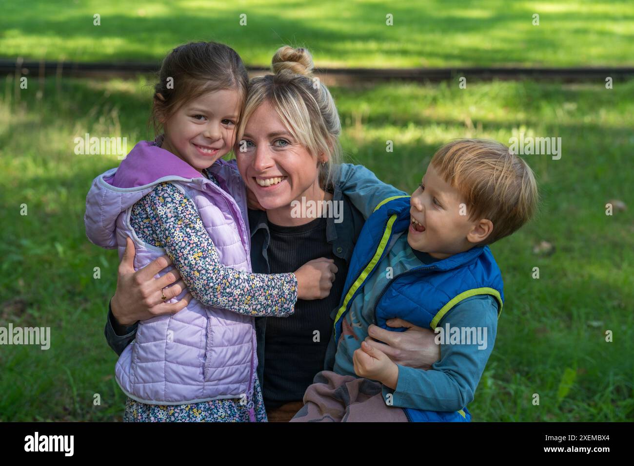 A young, modern mother gently hugs her daughter and son on a walk. Mom ...