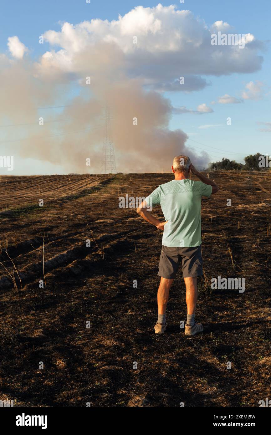 A man with his back turned looks concerned at his burnt field after the ...