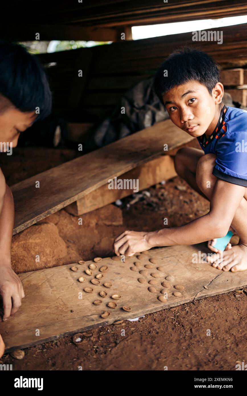 Two boys enjoy playing a game with shells on the ground in a village in ...