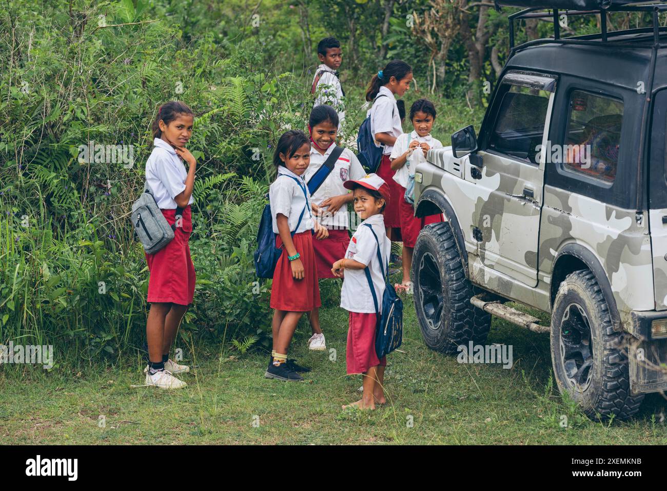 School children standing together by a parked SUV in West Sumba Regency ...