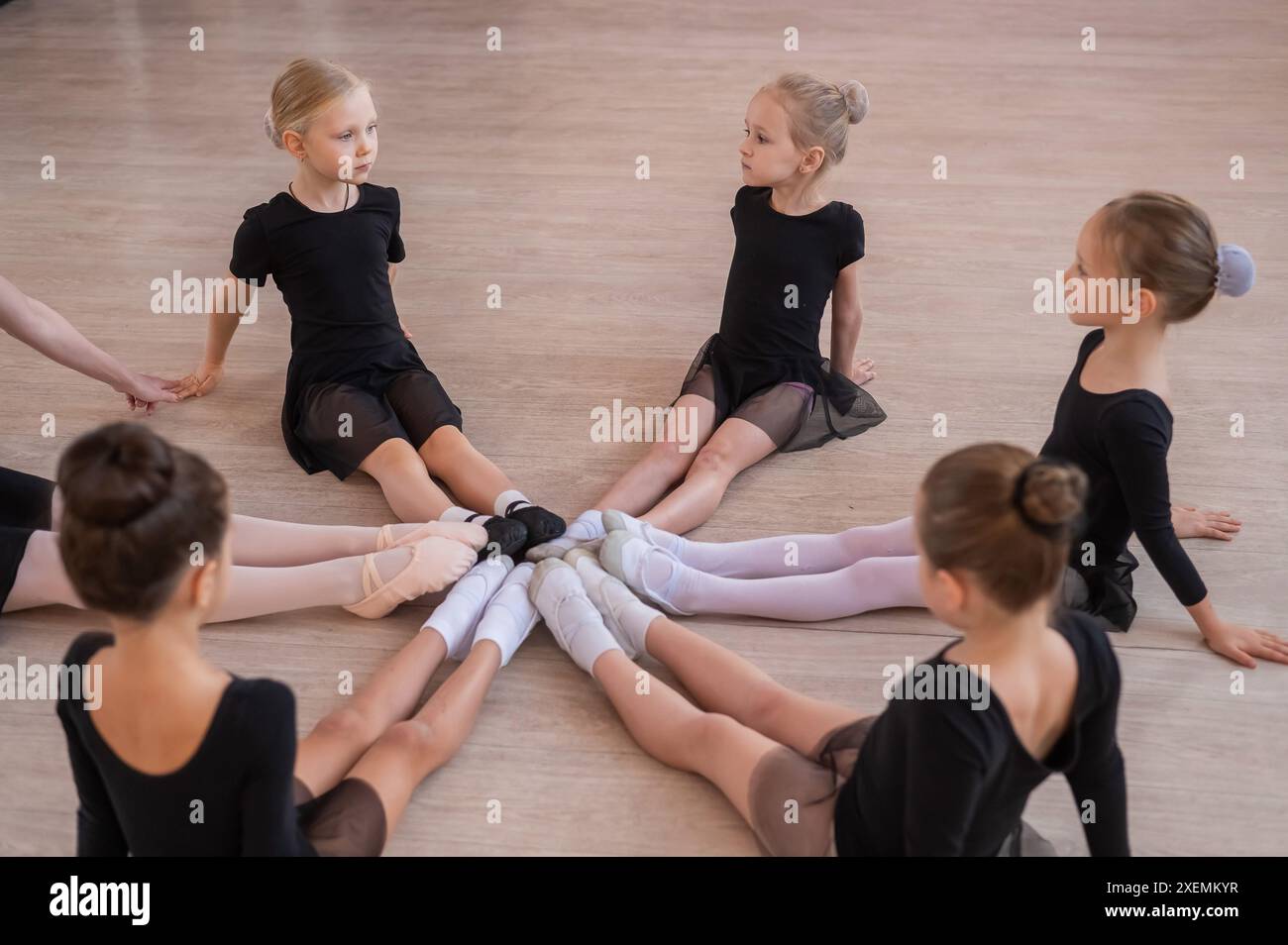 Caucasian woman and five little girls sit in a circle and do stretching ...