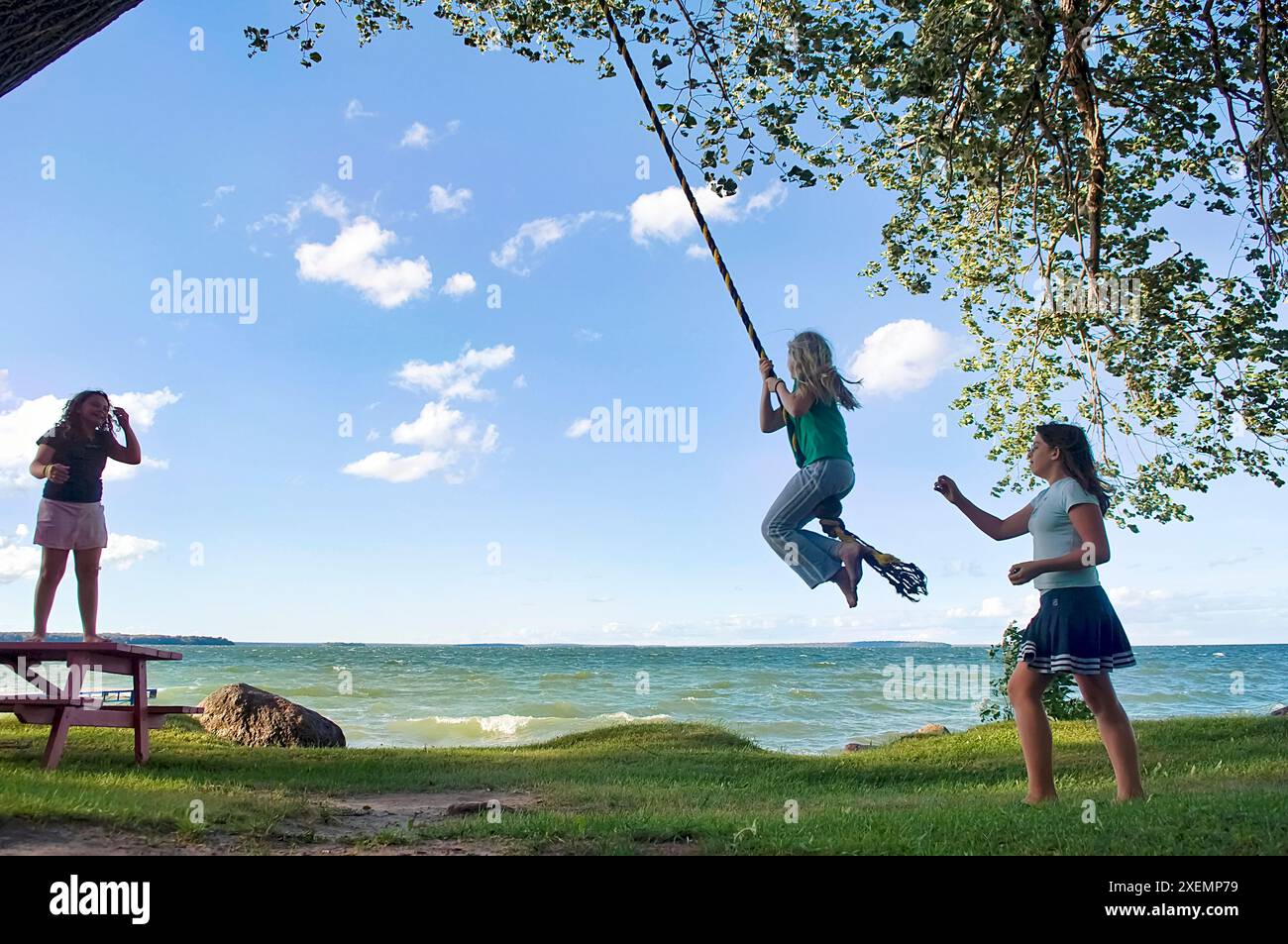 Three girls play on a rope swing along the shores of Leech Lake in ...
