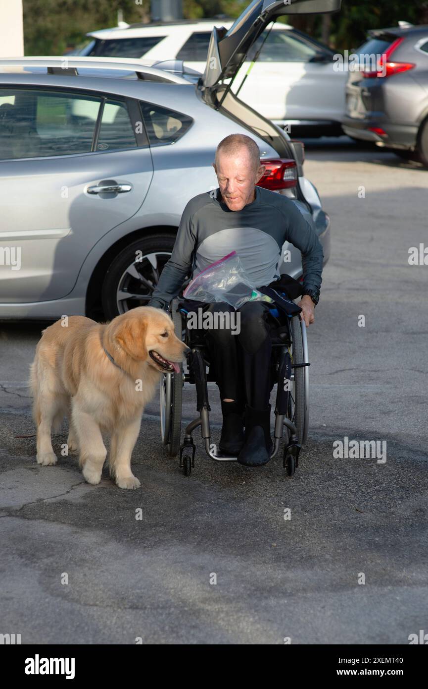 Paraplegic man in a manual wheelchair and his service dog in a parking ...