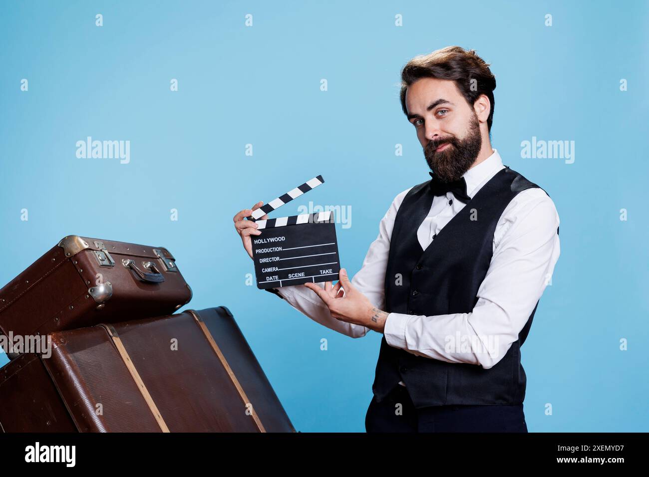 Young bellboy using filmslate in studio, acting like he is in movie ...