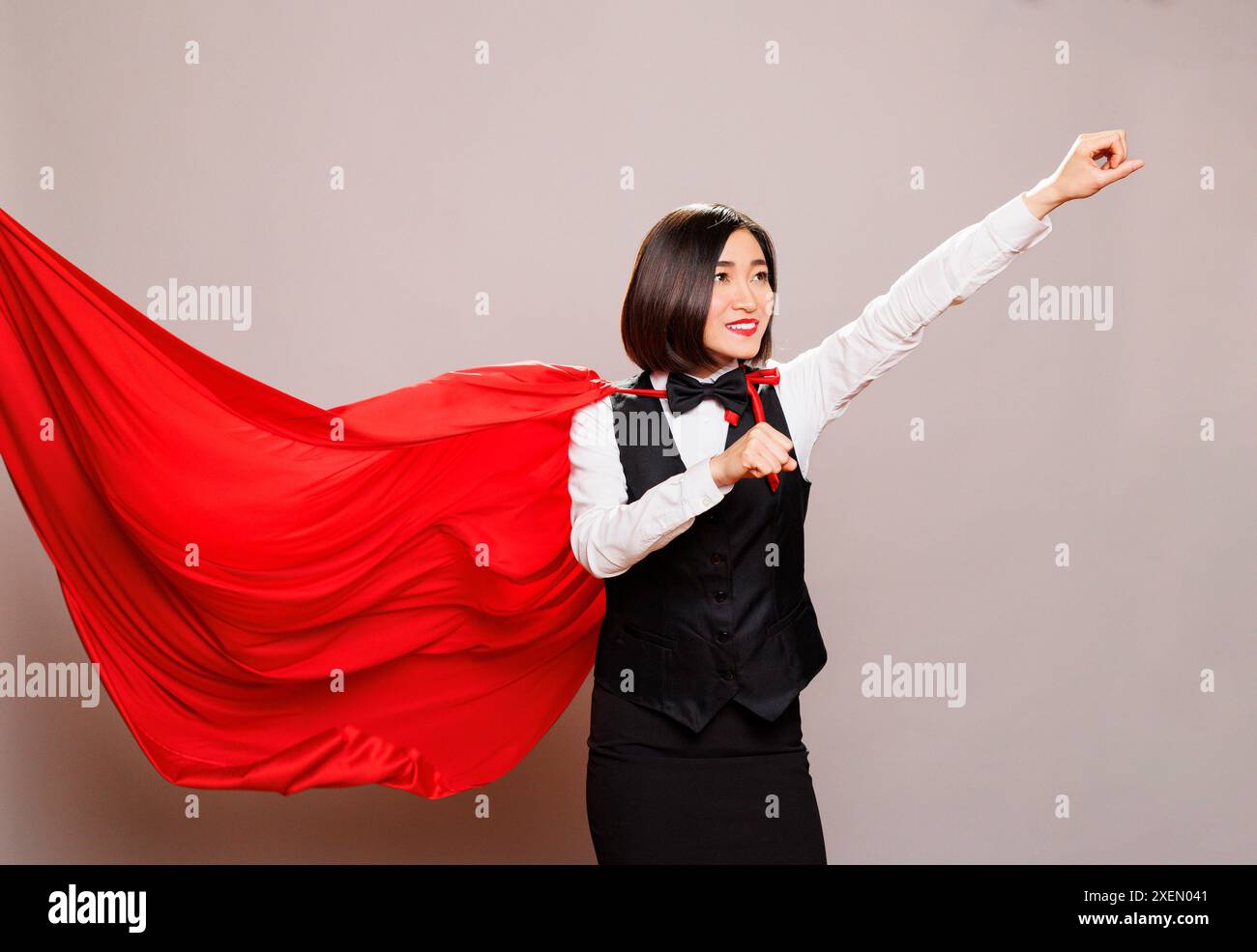 Cheerful asian woman wearing waitress uniform and superwoman cloak ...