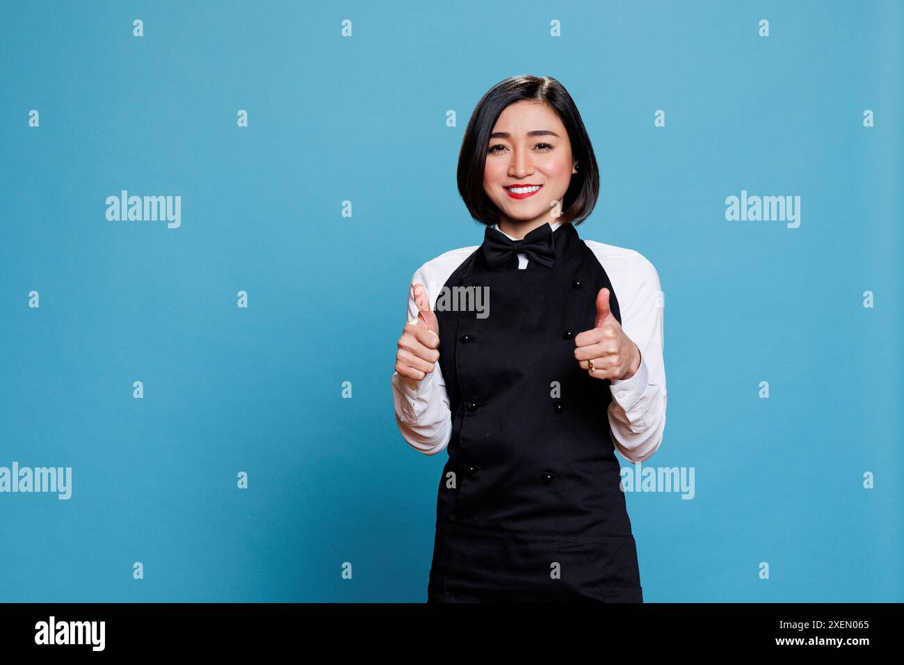 Smiling asian waitress wearing cafe uniform showing two thumbs up and ...