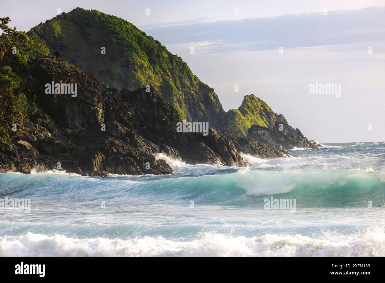 Rugged landforms covered in green vegetation and waves rolling into ...