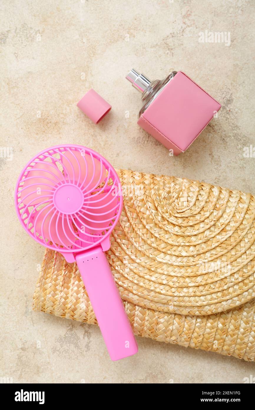 Portable pink electric fan, wicker purse, perfume and palm leaves on ...