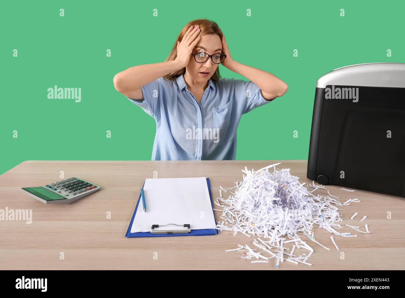 Shocked adult woman with shredder, shredded paper and clipboard sitting ...