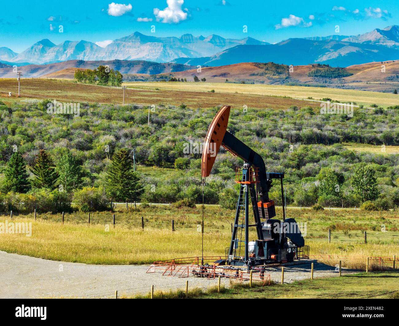 Pumpjack surrounded by trees, rolling hills and mountain range with a ...