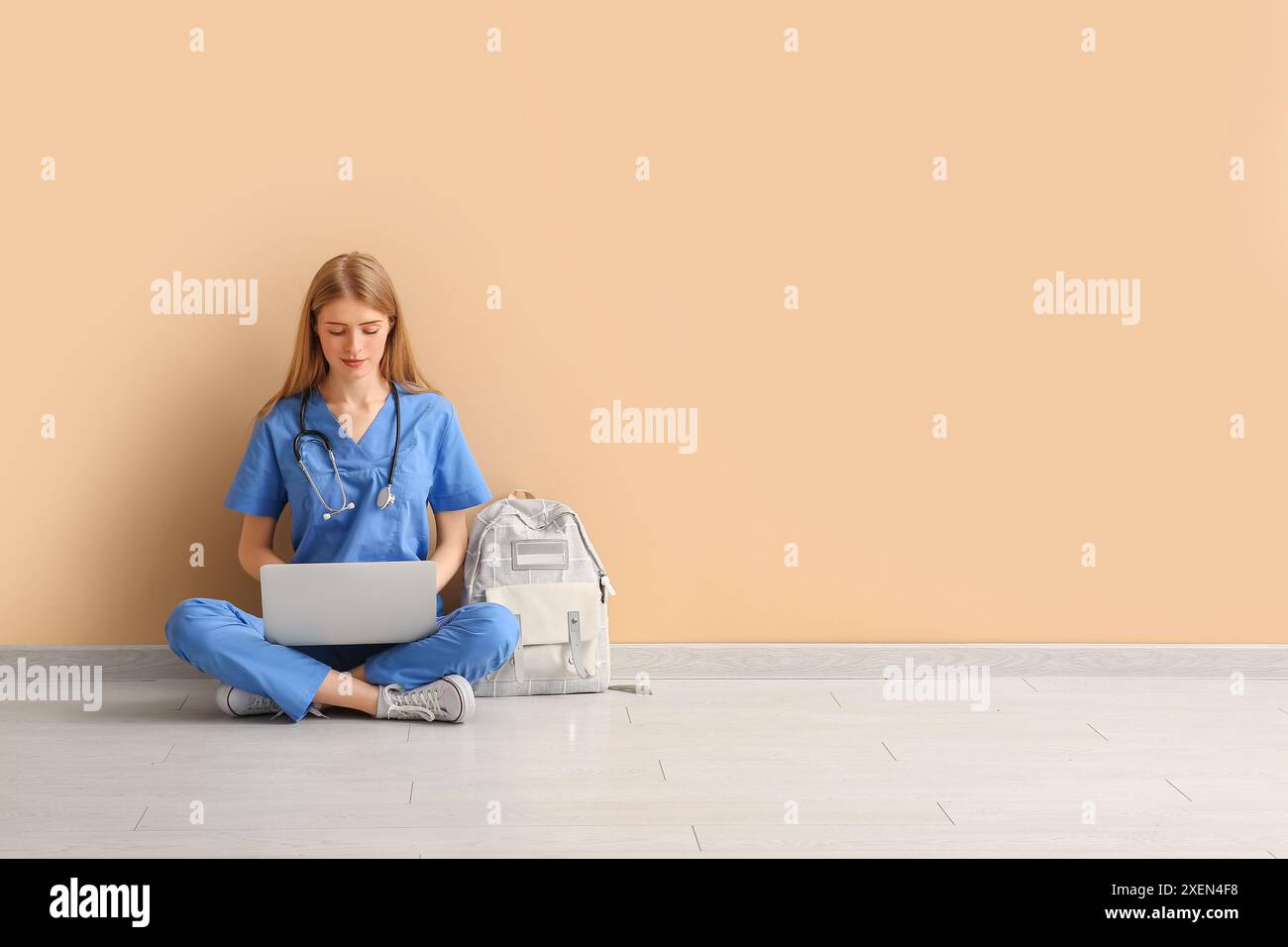 Female medical intern with laptop and backpack sitting on floor near ...