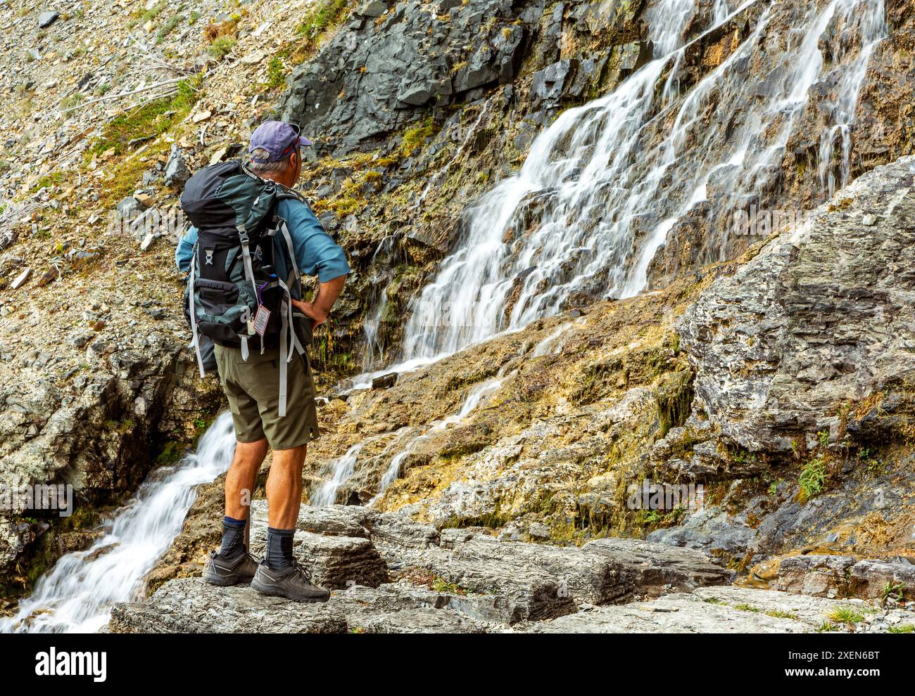 Male hiker overlooking a waterfall along a cliff face in Waterton Lakes ...