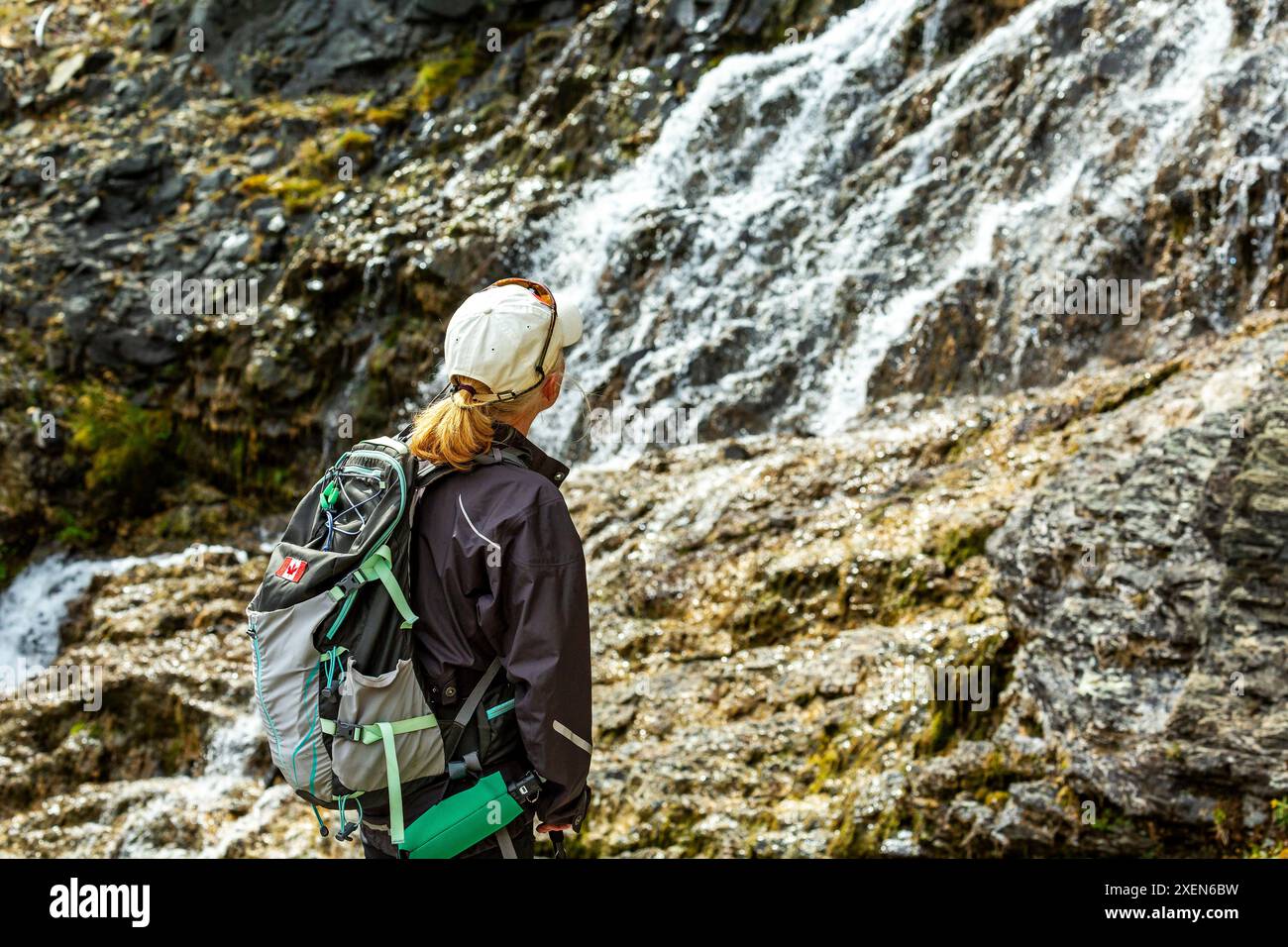 Female hiker overlooking a waterfall along a cliff face in Waterton ...