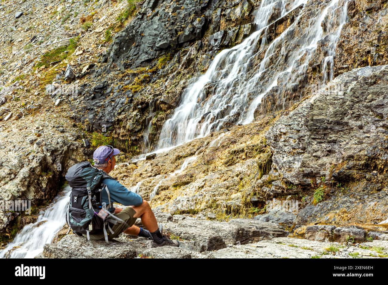 Male hiker overlooking a waterfall along a cliff face in Waterton Lakes ...