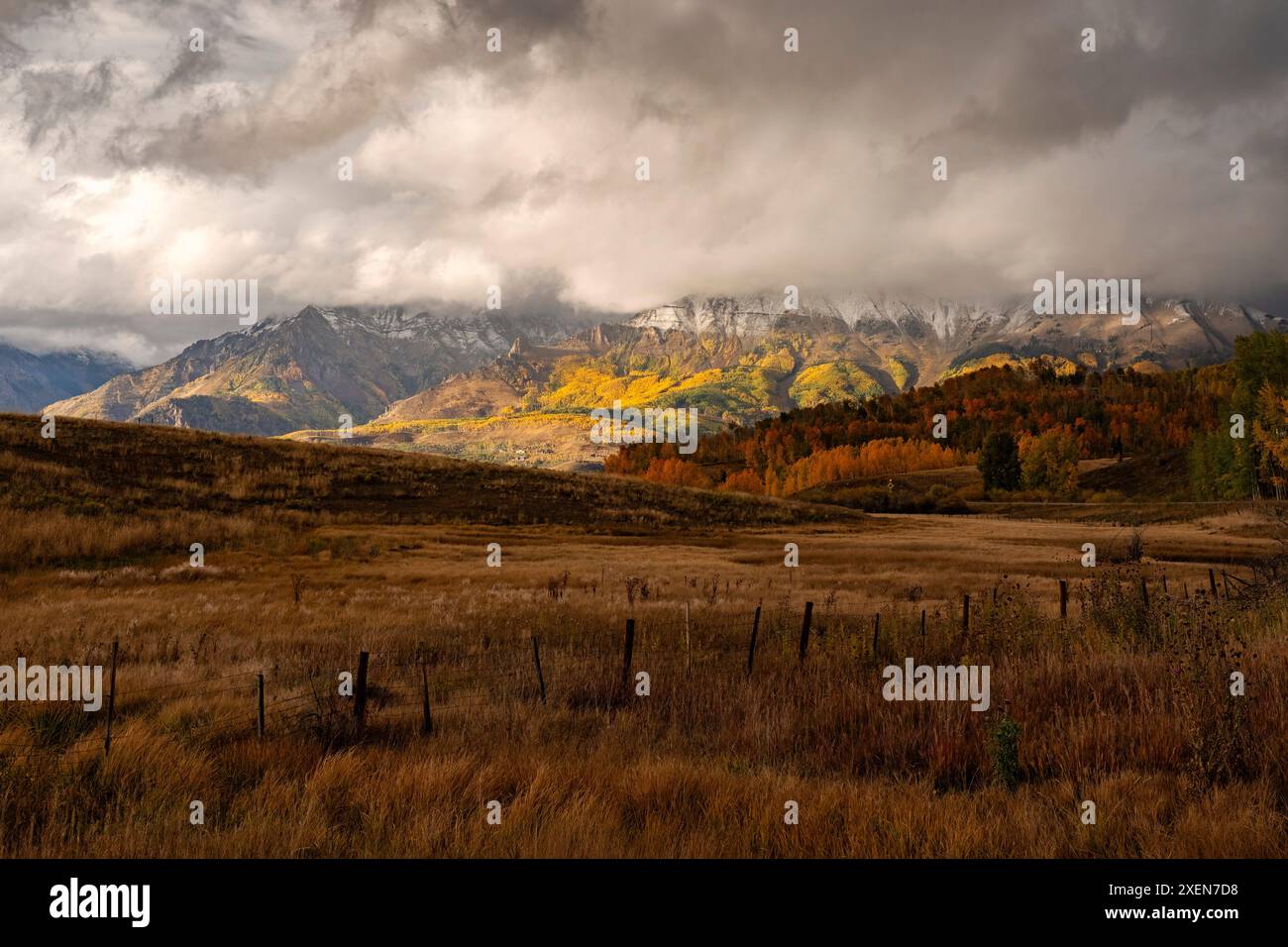Scenic vista of fall colors on the slopes of the snow-capped mountain peaks covered with stormy ...