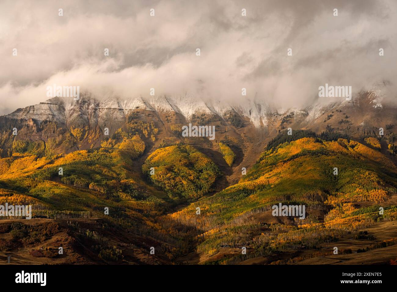 Scenic vista of fall colors on the slopes of the sunlit,snow-capped mountain peaks covered with ...
