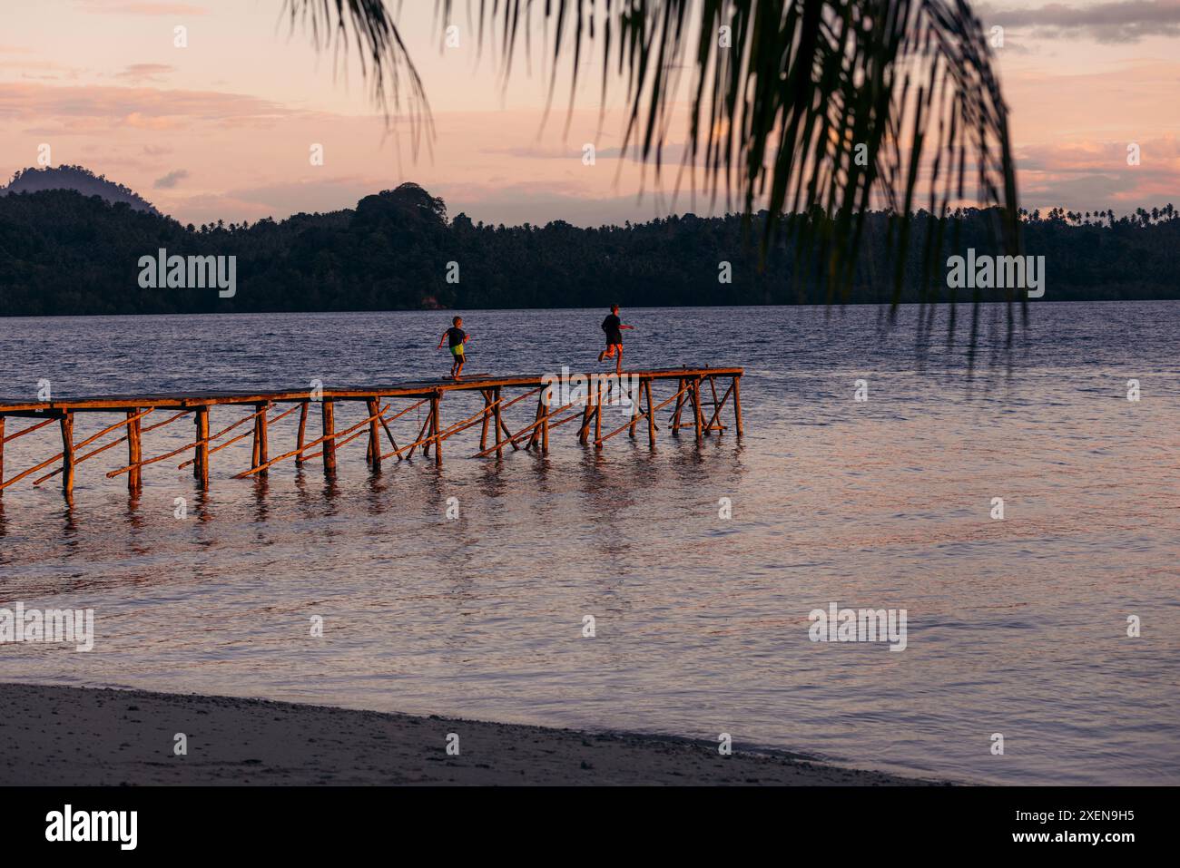 Boys run to the end of a dock at sunset at a resort on Bolilanga Island ...