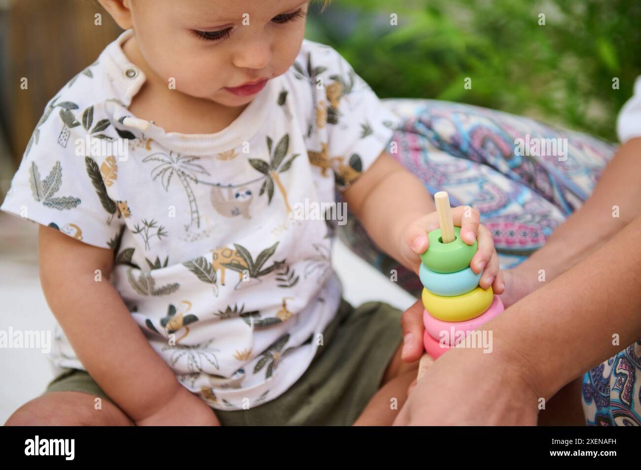 Selective focus on the hand of cute baby boy on colorful wooden circles of a pyramid, playing ...