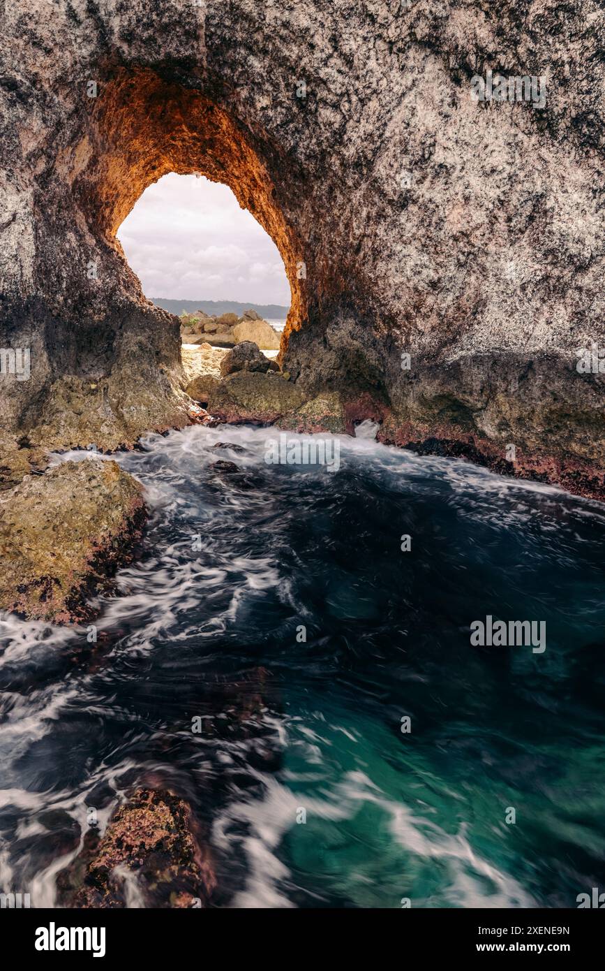 Surf flowing towards a natural arch along the beautiful rugged ...