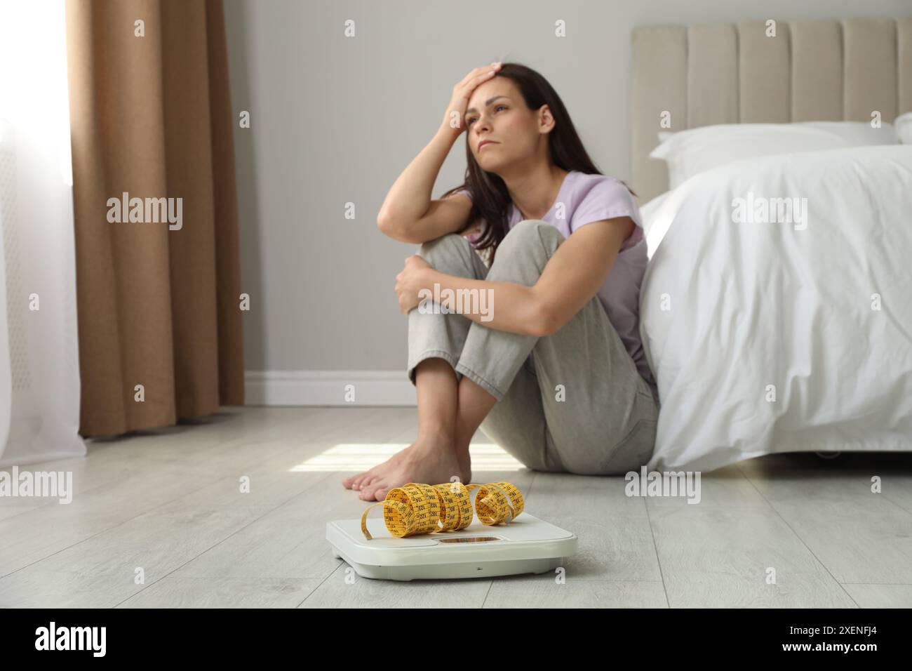 Eating disorder. Sad woman sitting near scale and measuring tape on ...