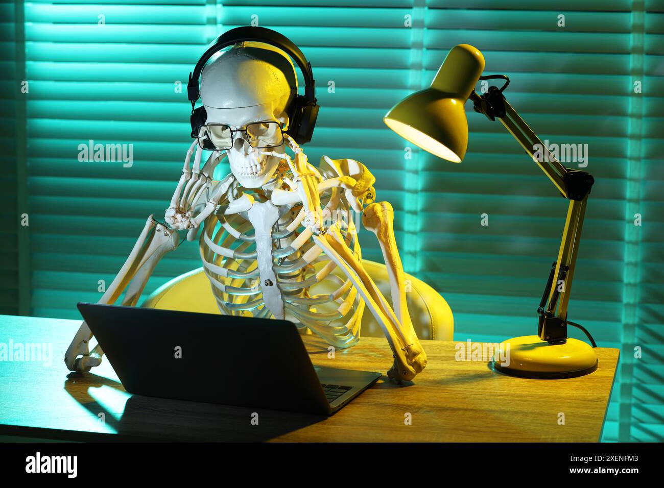 Waiting concept. Human skeleton sitting at wooden table with laptop and ...