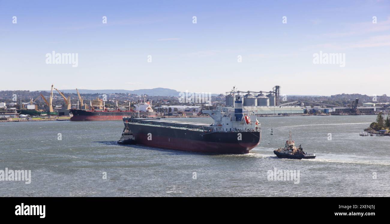 A large ship enters Newcastle Port with tug boats directing the way ...