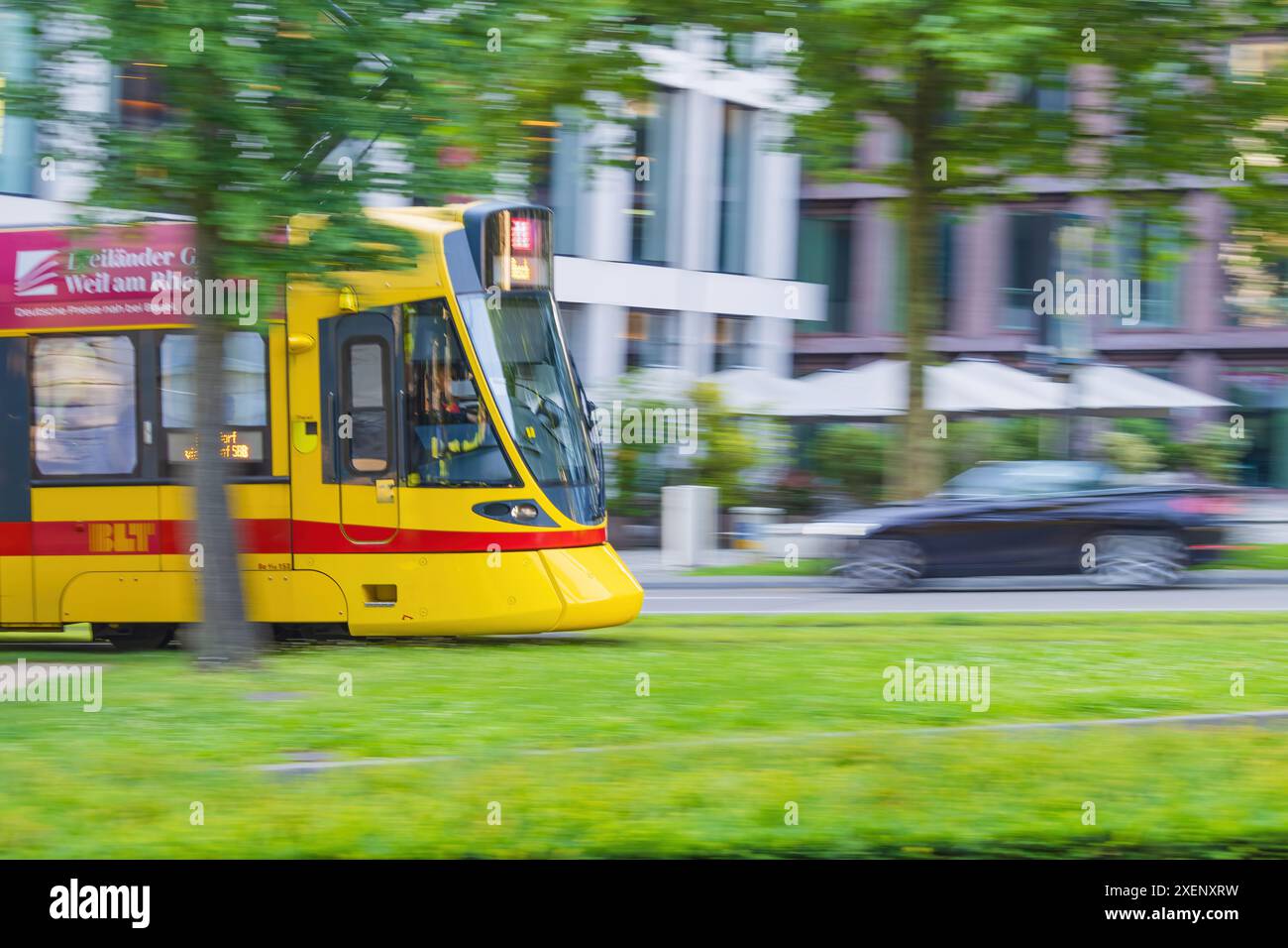 A yellow and red tram is driving down a street. The tram is on a city ...
