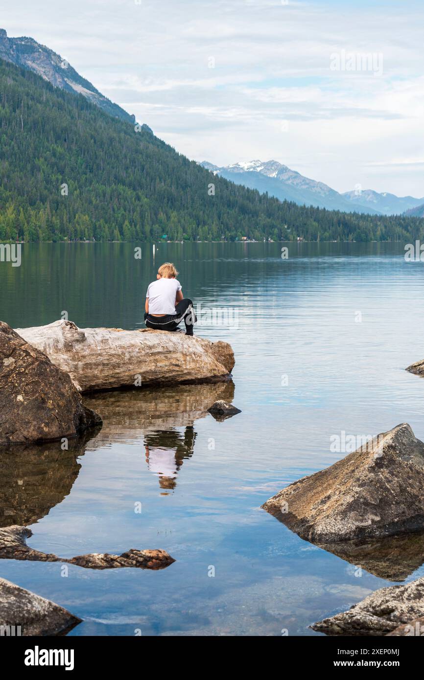 A vertical photo of a boy sitting on a log with his reflection in the ...