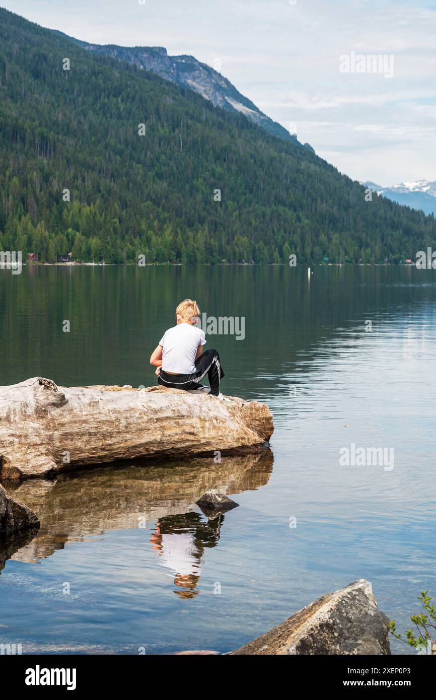 A vertical photo of a boy sitting on a log with his reflection in the ...