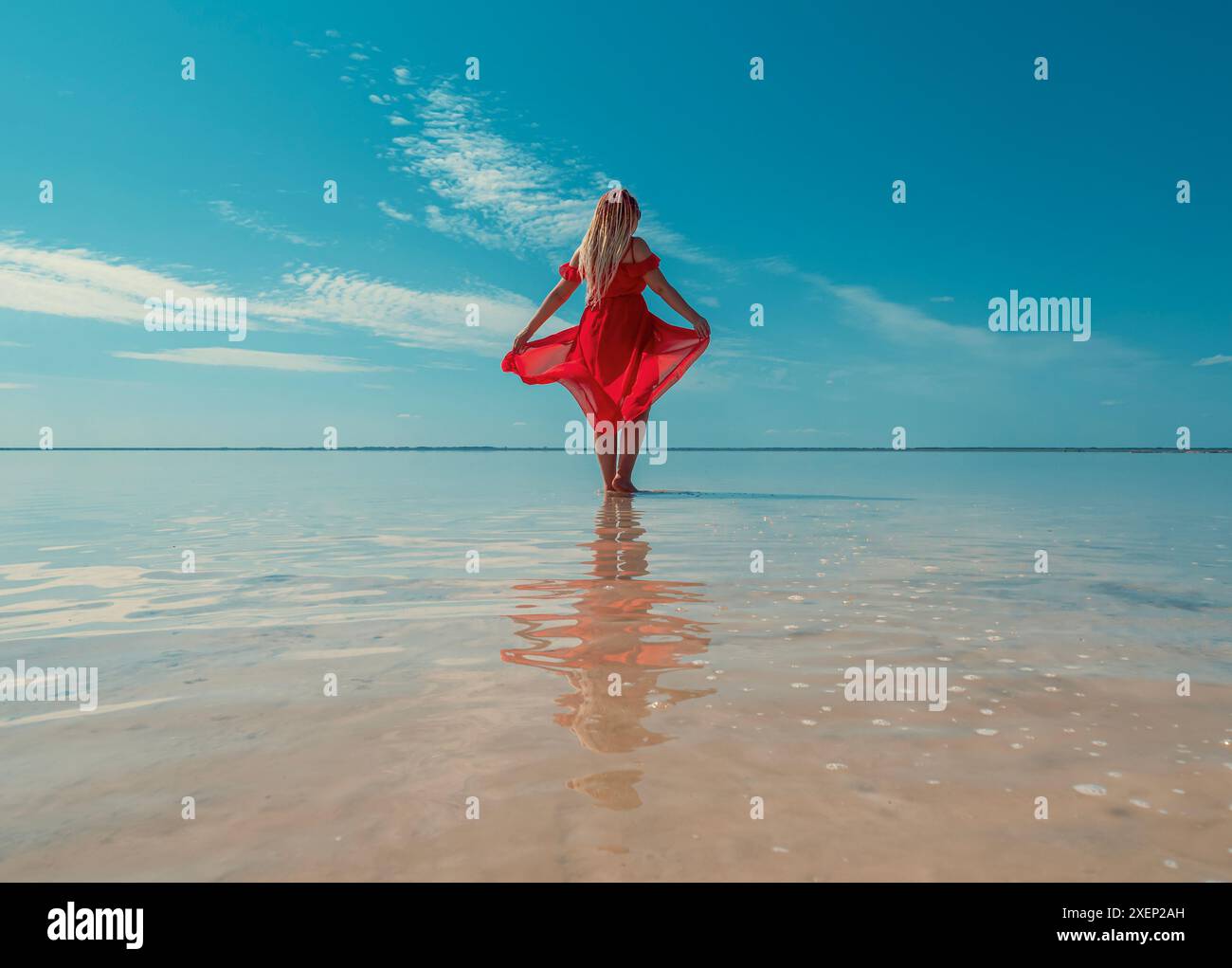 A woman in a red dress walks on the surface of a pink salt lake with ...