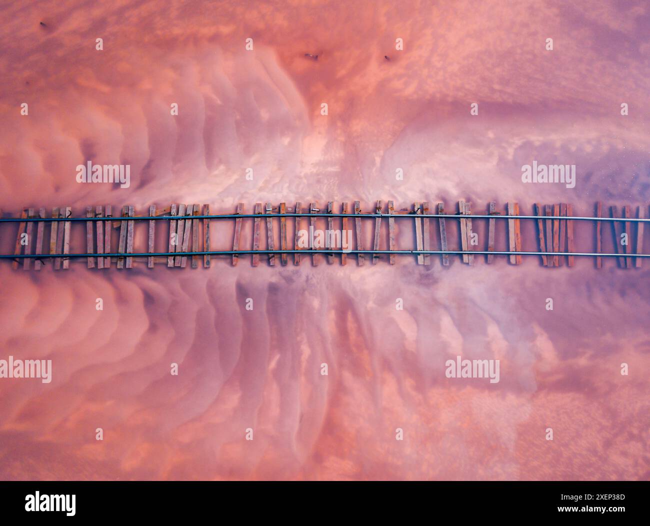 Aerial of a railroad tracks crossing a pink-hued lake. The perspective ...