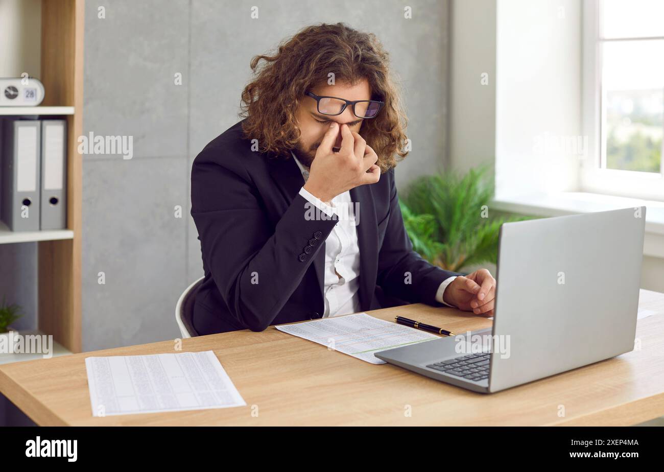 Tired man suffering from headache working on his workplace, massaging his nose bridge Stock ...