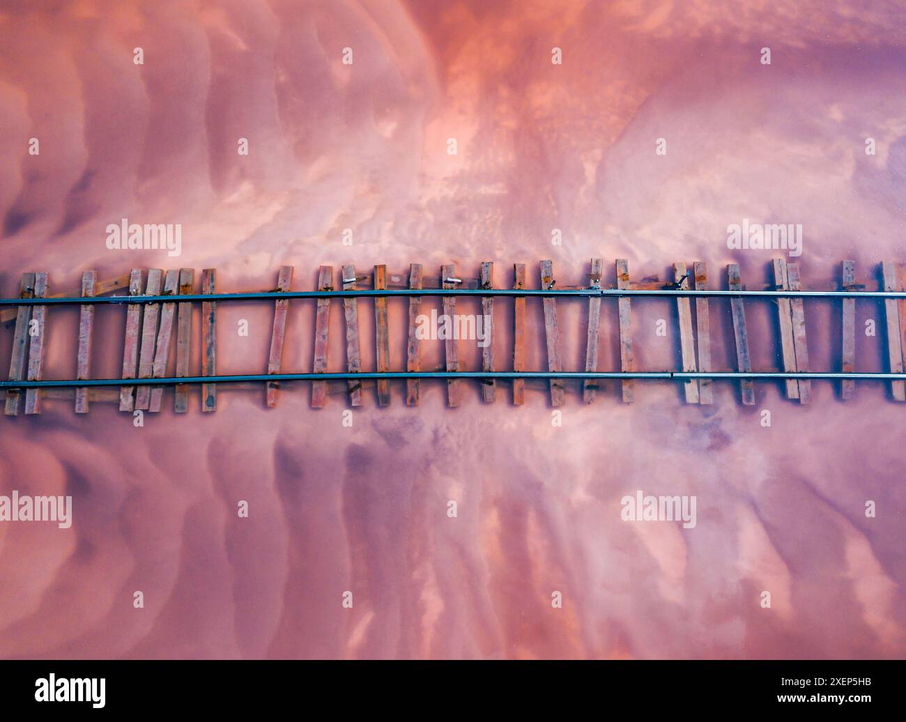 Aerial of a railroad tracks crossing a pink-hued lake. The perspective ...